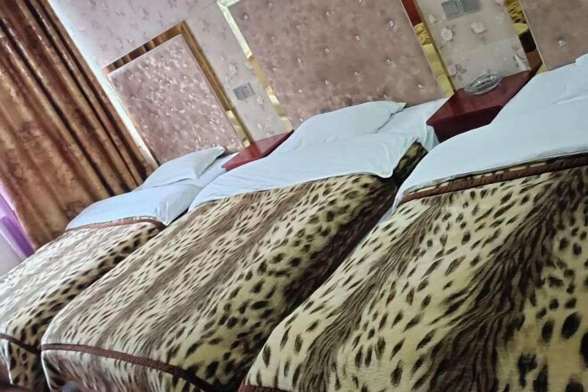 Uma cama com roupa de cama em padrão de leopardo, um criado-mudo vermelho com um objeto de vidro e uma parede estampada.