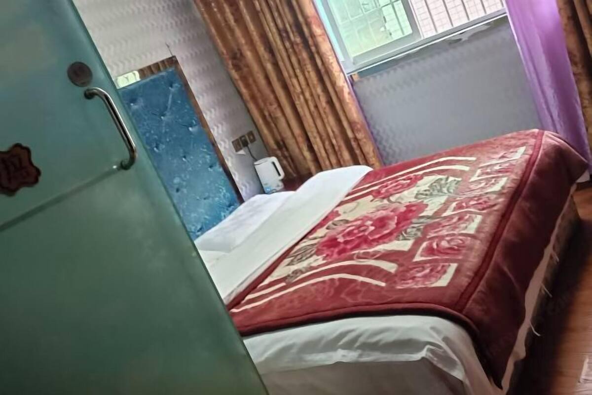 Um quarto com uma cama, um guarda-roupa, uma janela com cortinas e uma chaleira no criado-mudo.