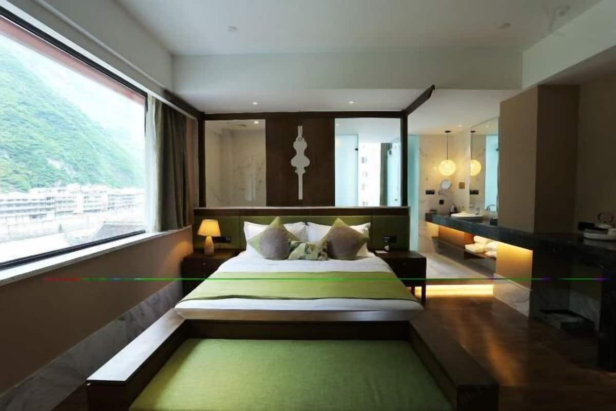 Quarto de hotel moderno com uma cama grande, uma mesa de cabeceira, um espelho e vista para uma montanha.
