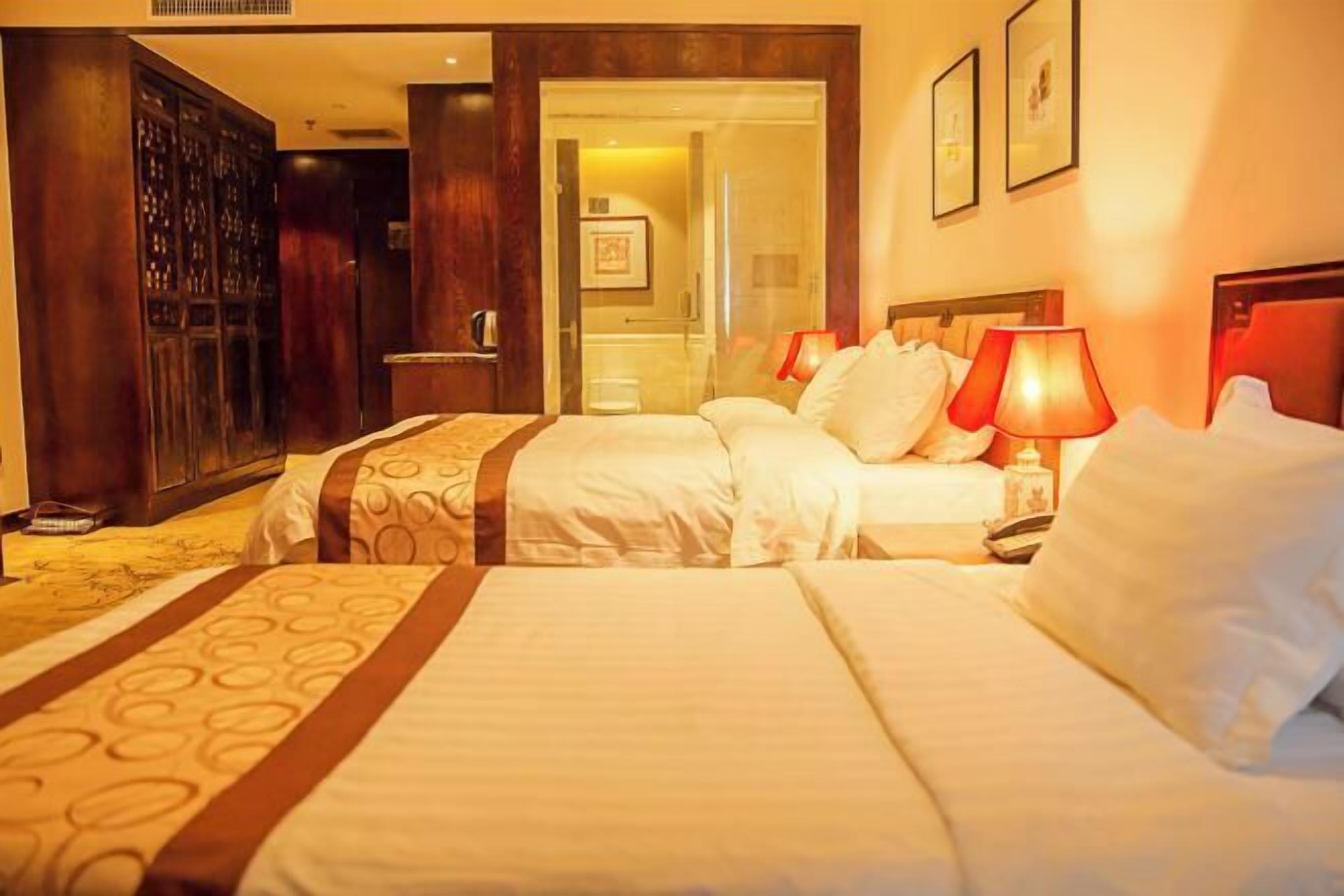 Quarto de hotel com duas camas, um guarda-roupa, um espelho e uma porta que dá para outro cômodo.