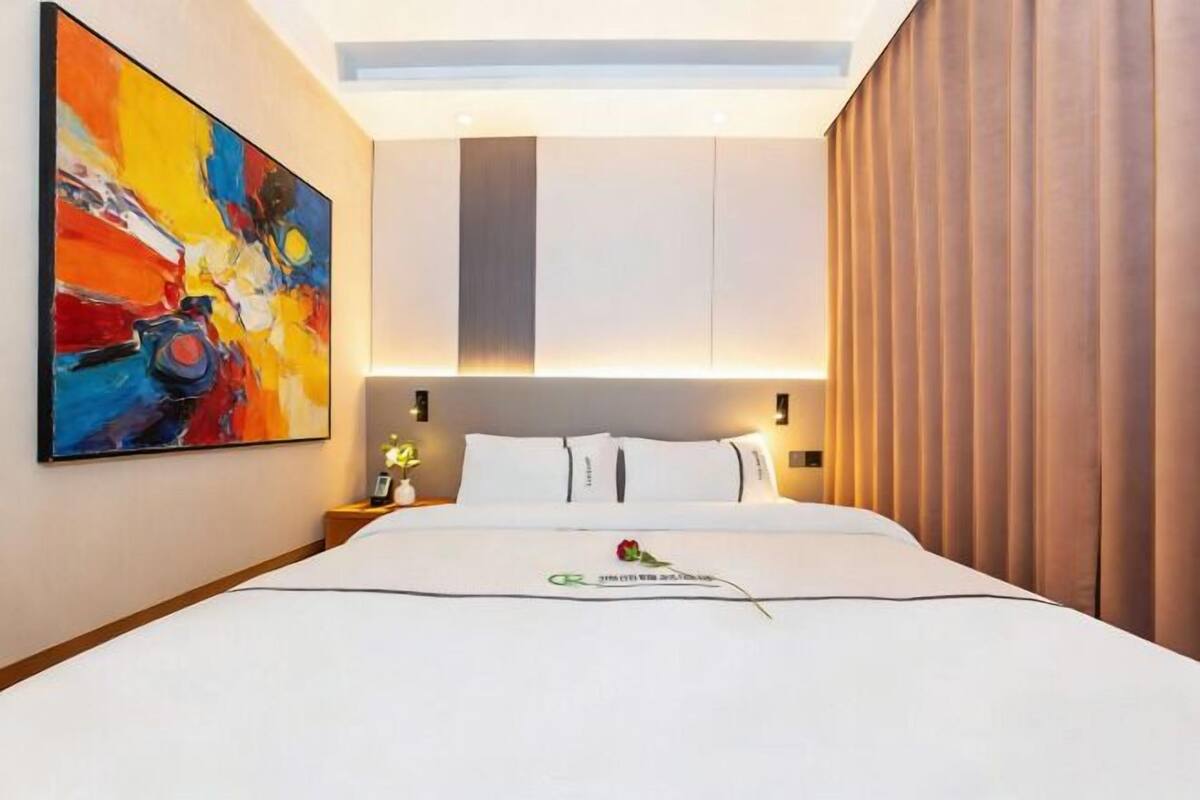 Quarto de hotel moderno com uma cama grande, um quadro na parede e vista para a cidade.