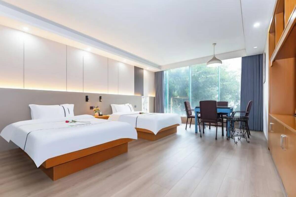 Quarto de hotel moderno com duas camas, uma mesa de jantar com cadeiras e grandes janelas com vista para o exterior.
