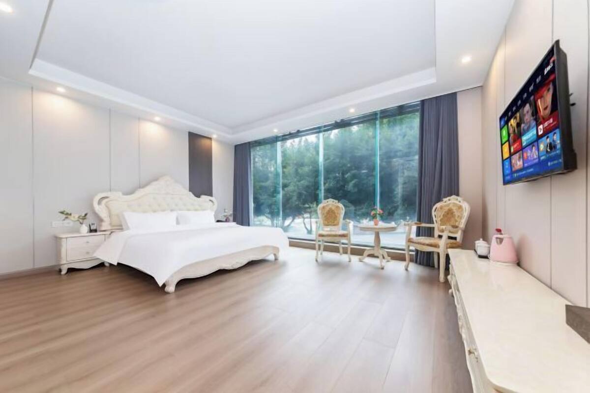 Quarto moderno com uma cama grande, uma mesinha, duas cadeiras e uma TV fixada na parede.