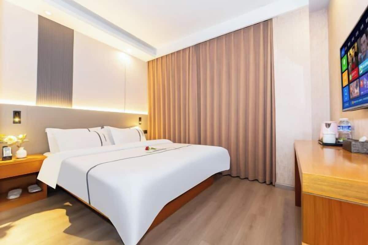 Quarto de hotel com uma cama, uma escrivaninha de madeira, um criado-mudo e uma televisão fixada na parede.