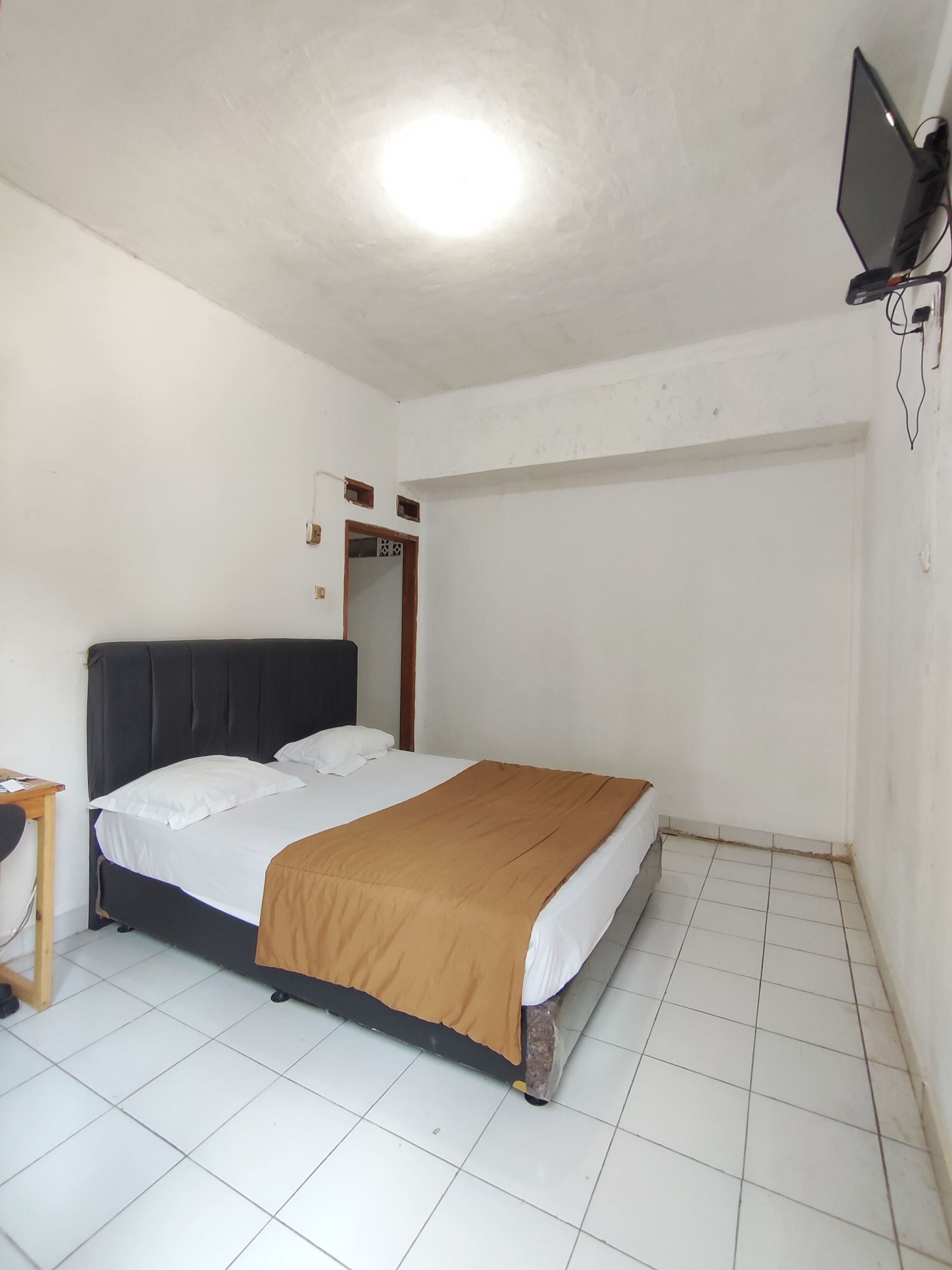 Quarto com cama, escrivaninha e televisão na parede.