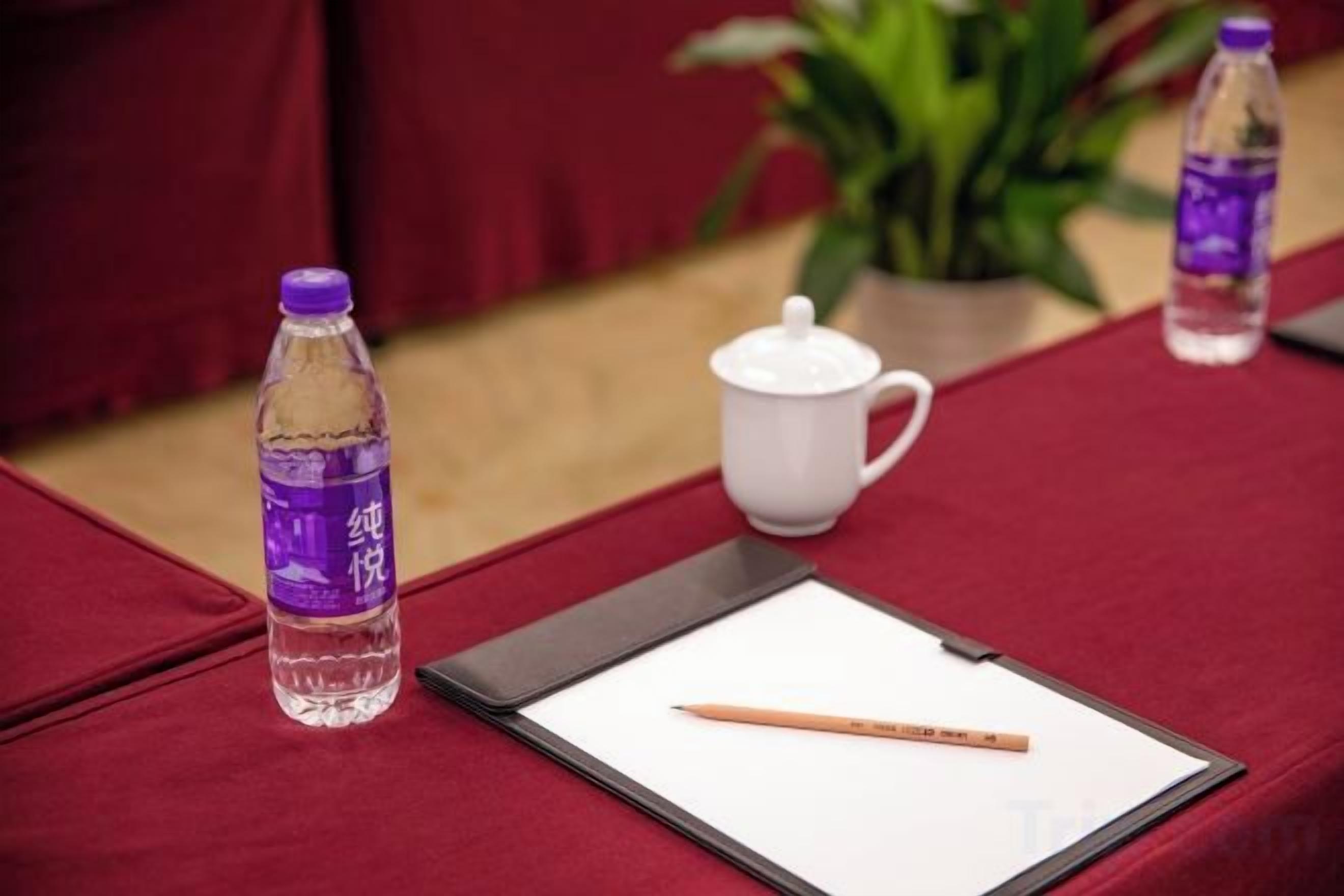 Uma mesa com uma garrafa de água, uma caneca branca, um tablet e um lápis.