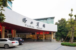 Entrada de hotel com design moderno, apresentando uma grande placa com caracteres chineses e o nome 'Tashan Hotel' em inglês.