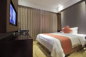 Quarto de hotel com cama, televisão sobre um suporte e cortina.
