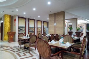 Um espaço de refeições de hotel com várias mesas e cadeiras, um pilar grande e vista para o exterior.