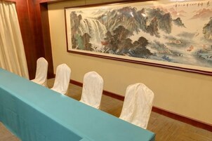 Quarto com uma mesa comprida coberta por panos brancos, um quadro grande emoldurado na parede e um corrimão azul.
