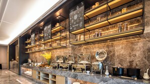 Disposição de buffet com diversas estações de serviço, bancada de mármore e variedade de recipientes para alimentos e bebidas.