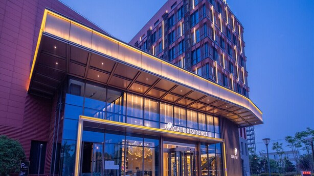 Uma entrada de hotel moderna com fachada de vidro, uma cobertura de entrada destacada e uma placa com a inscrição "GAPE RESIDENCE".