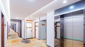 Corredor de hotel com várias portas, um elevador e piso estampado.