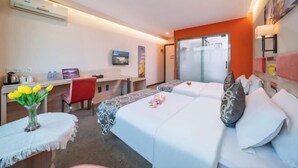 Quarto de hotel com uma cama, uma escrivaninha, uma cadeira, uma mesinha com um vaso de flores e uma janela.
