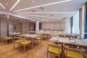 Ampla sala de jantar com várias mesas e cadeiras, um buffet central e grandes janelas que permitem entrada de luz natural.