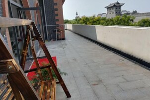 Terraço no telhado com vista para um edifício tradicional, uma escada de madeira e alguns vasos com plantas.