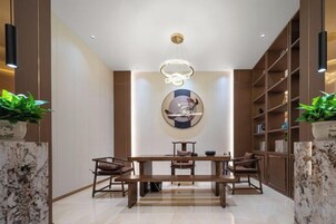 Uma sala de jantar moderna com bancada de mármore, mesa de jantar de madeira e cadeiras. Há uma grande obra de arte circular na parede e uma estante à direita.