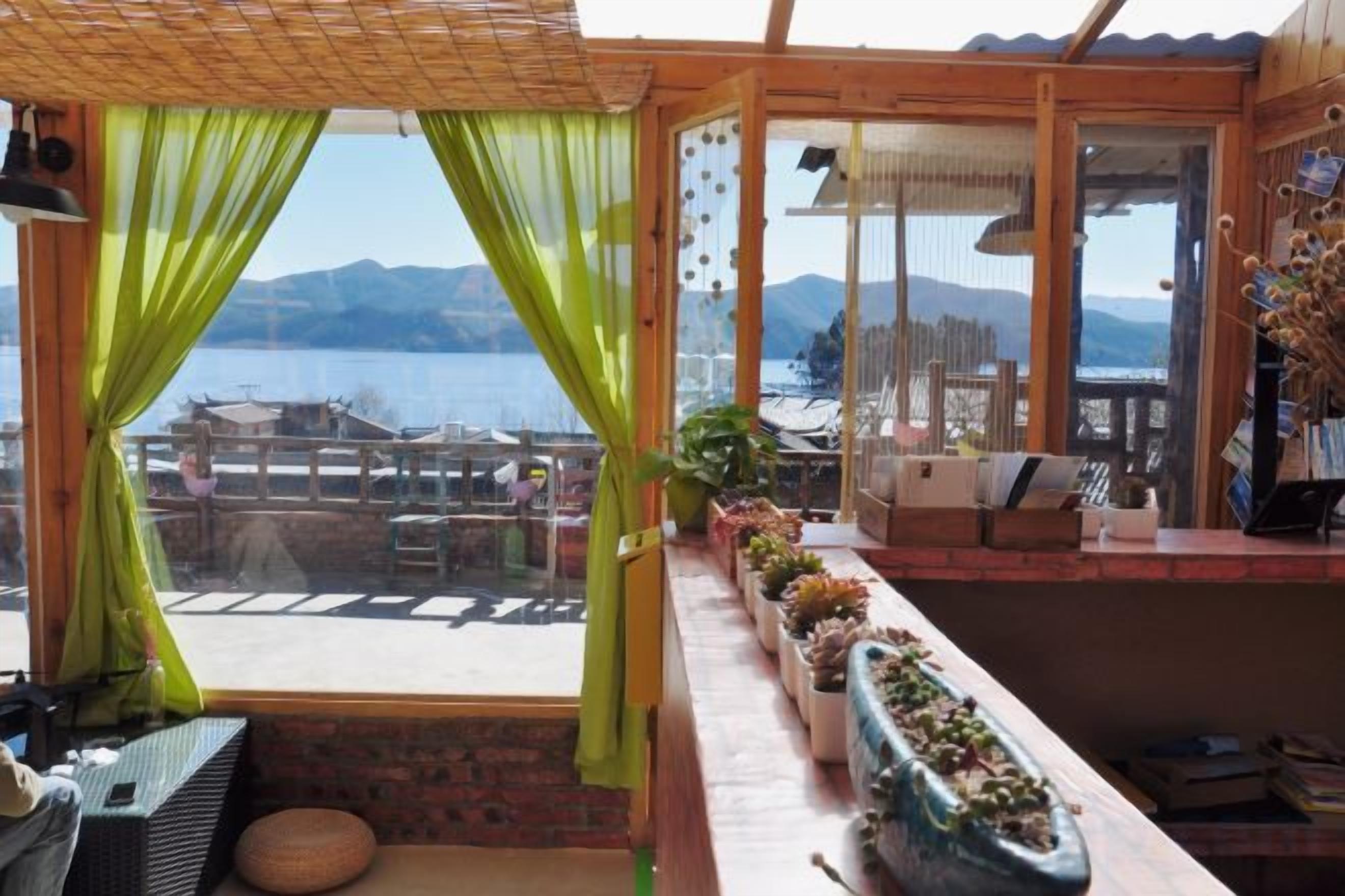 Quarto com vista para um lago e montanhas, teto de madeira e uma janela comprida com cortinas.