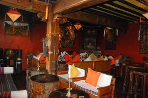 Quarto tradicional com cama de madeira, uma pequena mesa e uma cadeira. Há diversos objetos decorativos e um quadro grande na parede.