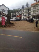 Um edifício com vários andares e varandas, um estacionamento com diversos carros e uma placa.