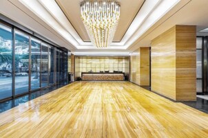 Um hall espaçoso com piso de madeira envernizada, balcão de recepção e um grande candelabro.