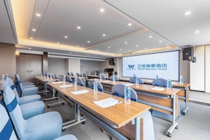 Sala de conferência com uma mesa comprida, cadeiras e tela de projeção.