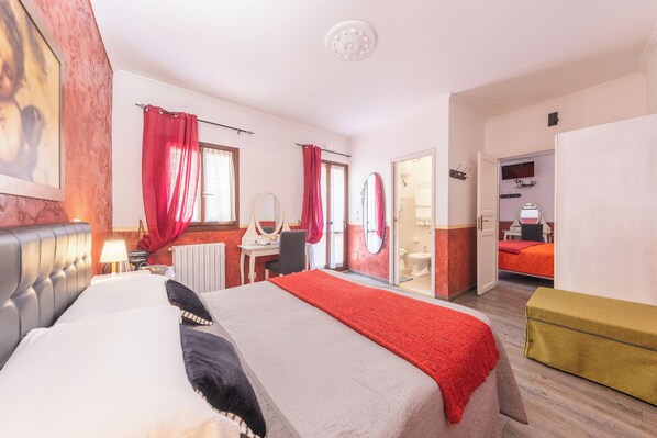 Quarto de hotel com uma cama grande, uma escrivaninha, uma cadeira, um espelho e um banheiro visível através de uma porta aberta.