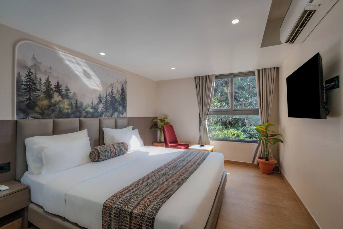 Quarto de hotel com uma cama grande, televisão montada, janela com cortinas e um quadro na parede.