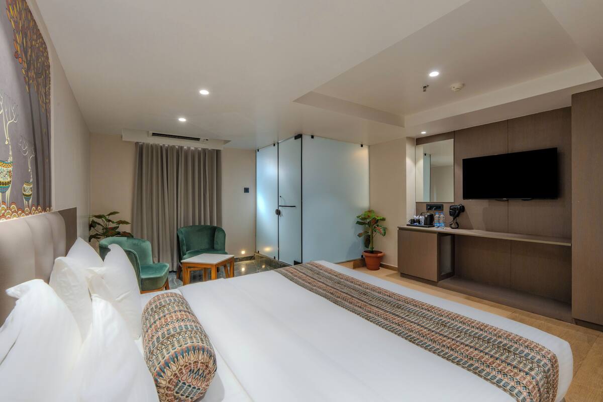 Quarto de hotel com uma cama grande, uma escrivaninha, uma cadeira, uma televisão e um guarda-roupa.