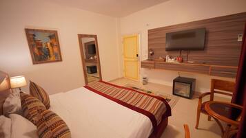 Quarto de hotel com uma cama, televisão, armário de madeira, cadeira e um pequeno aquecedor.