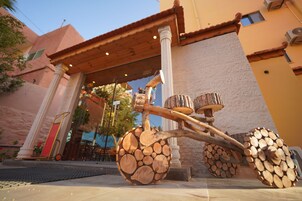 Entrada de um edifício com estrutura de madeira que lembra um carrinho, troncos e um carrinho de transporte metálico.