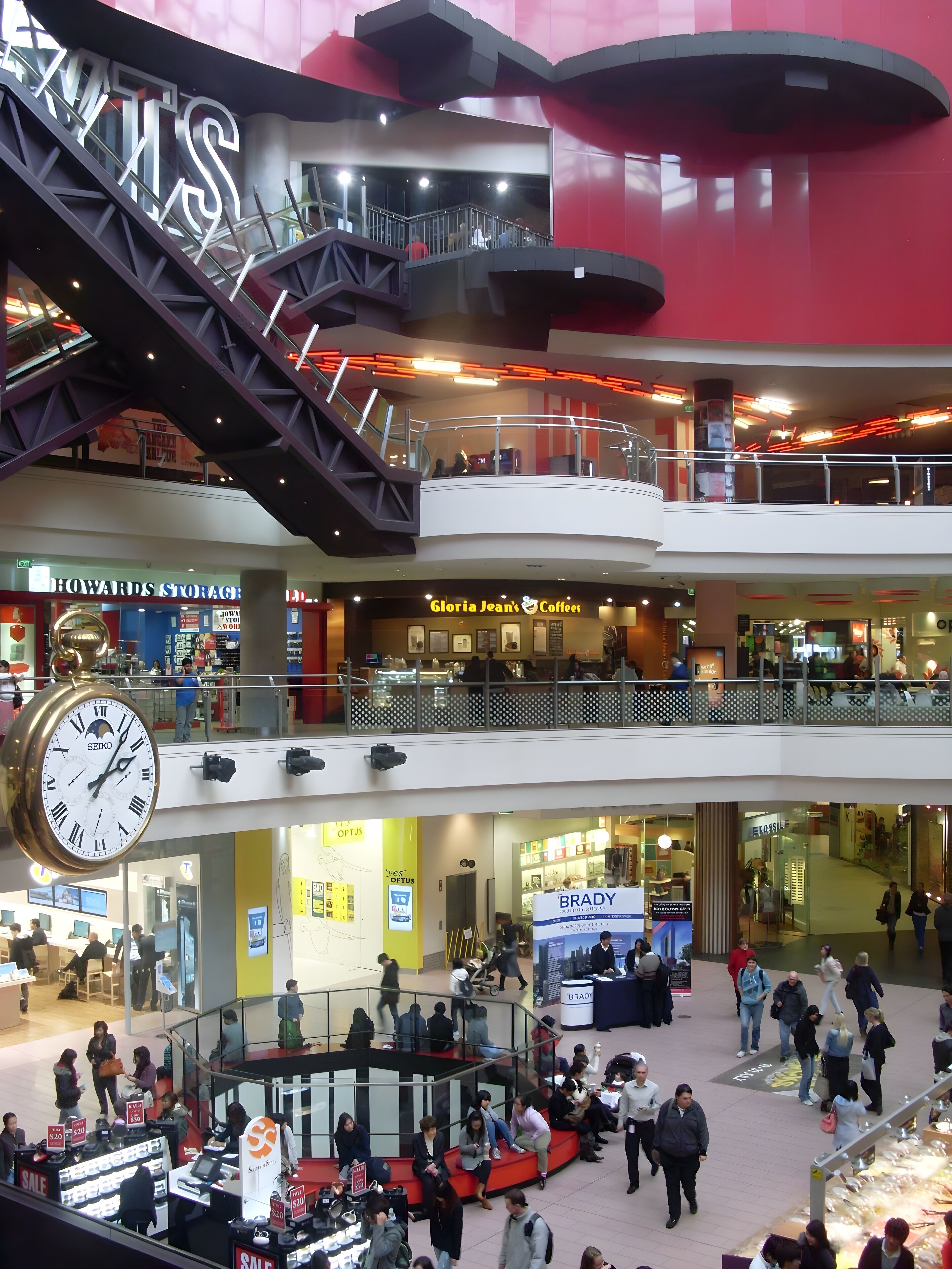 Um centro comercial com vários níveis e diversas lojas, incluindo uma joalheria e uma cafeteria.