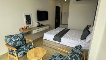 Quarto de hotel moderno com cama, duas cadeiras, uma mesinha, televisão e ar condicionado.