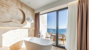 Um banheiro moderno com uma banheira de pedestal, uma janela grande com cortinas e vista para o mar.