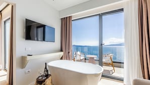 Uma casa de banho moderna com uma banheira independente, uma televisão montada e uma varanda com vista para o mar.