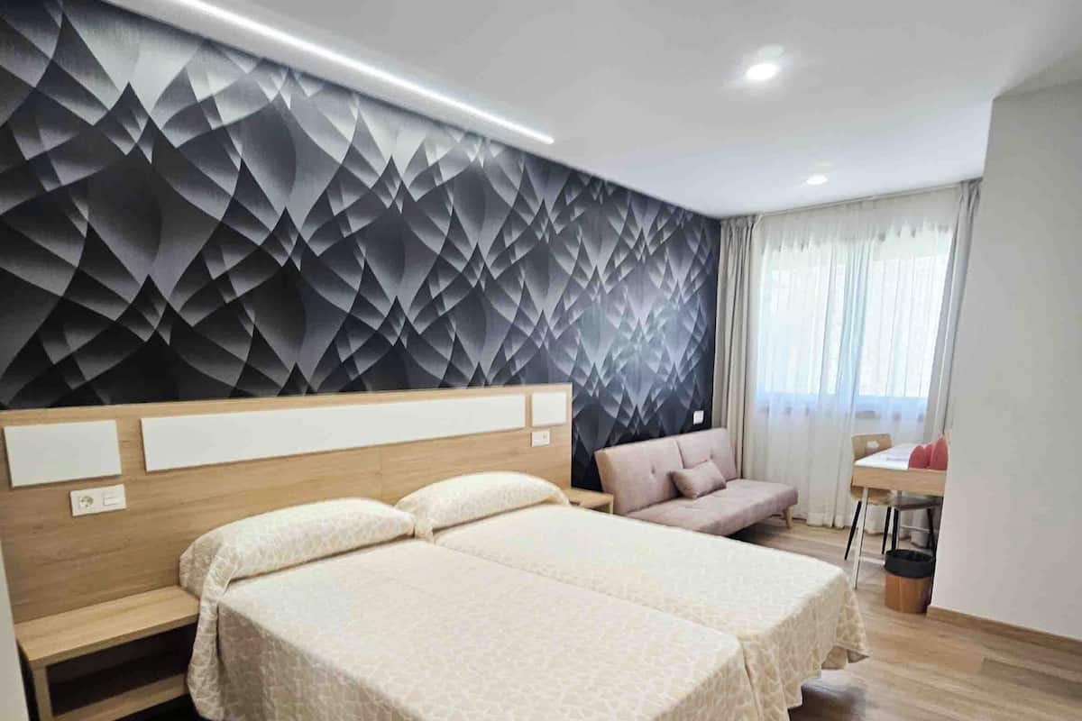 Quarto de hotel com duas camas, um sofá, uma escrivaninha e uma parede estampada.