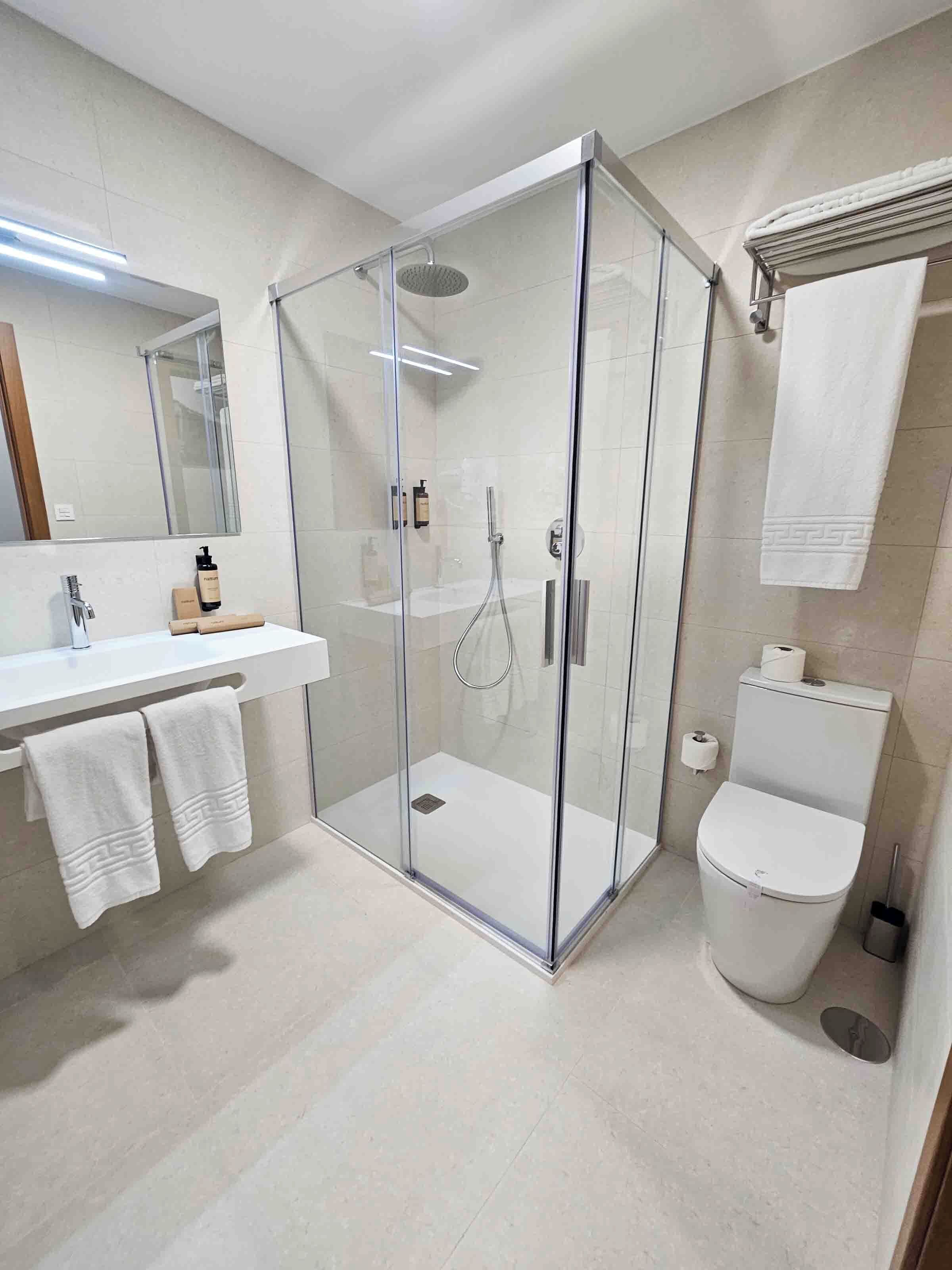 Uma casa de banho moderna com chuveiro em cabine de vidro, lavatório branco com espelho e sanita.