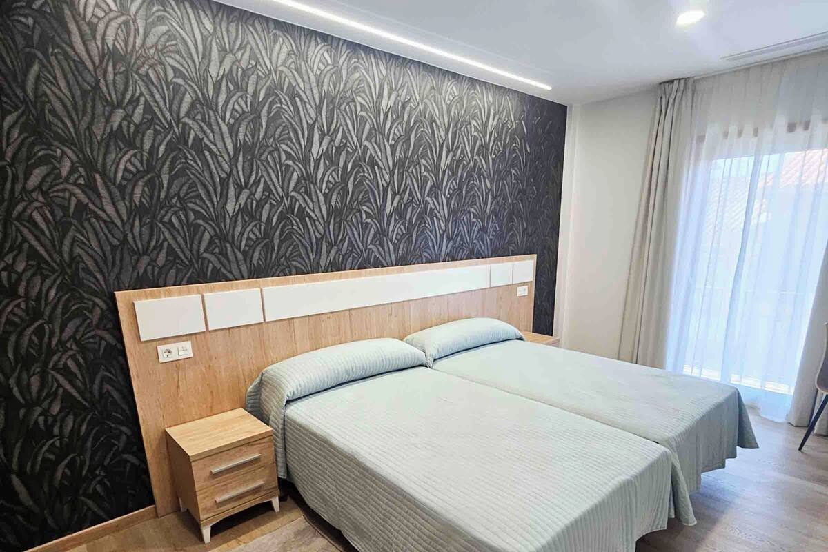 Quarto moderno com uma cama grande, uma mesinha de cabeceira e um papel de parede estampado.