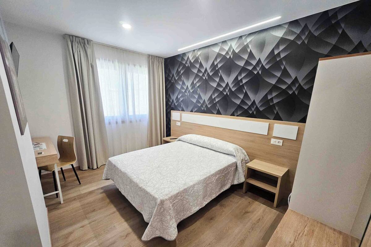 Quarto de hotel moderno com cama de madeira, uma secretária e uma cadeira.
