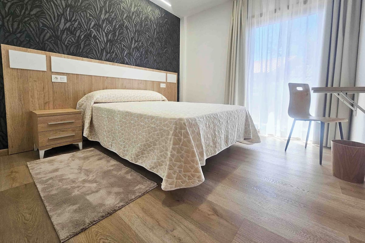 Quarto de hotel com cama, mesa de cabeceira, escrivaninha e cadeira.