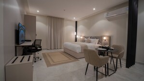 Quarto de hotel moderno com cama, escrivaninha, cadeira e um pequeno espaço de refeições.
