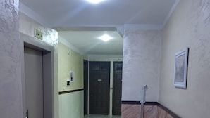 Um corredor com piso de mármore, uma porta à esquerda e um quadro na parede direita.