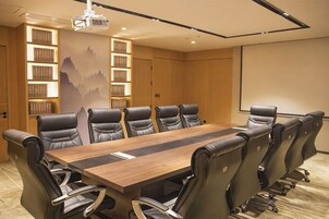 Sala de conferências com uma mesa comprida e oito cadeiras, um projetor e estantes.