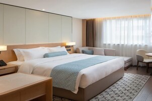 Quarto de hotel com uma cama grande, mesas de cabeceira, escrivaninha, cadeira e janela com cortinas.