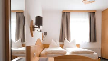 Quarto de hotel com duas camas, uma mesa de cabeceira, uma luminária e uma janela com cortinas.