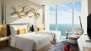 Quarto de hotel moderno com duas camas, uma escrivaninha, uma cadeira e vista para o mar.