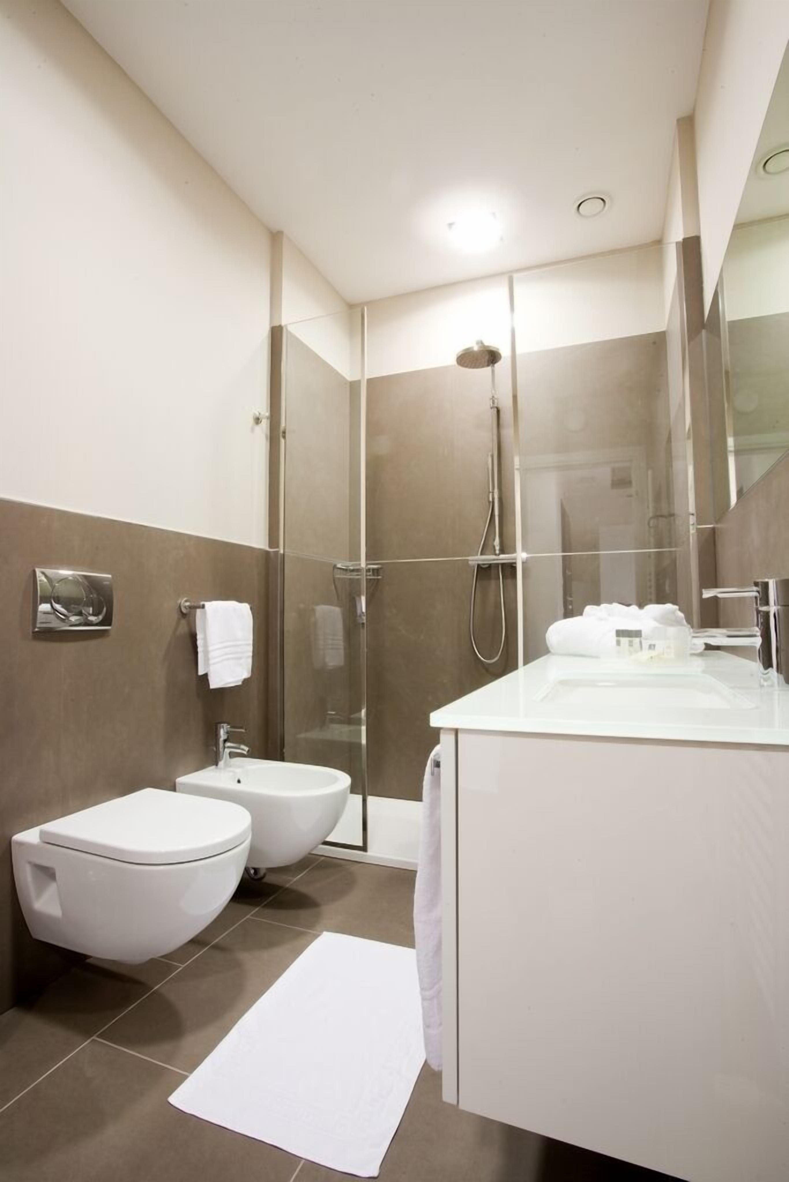 Uma casa de banho moderna com chuveiro de vidro, uma sanita branca e um bidé.