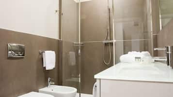 Uma casa de banho moderna com chuveiro de vidro, uma sanita branca e um bidé.