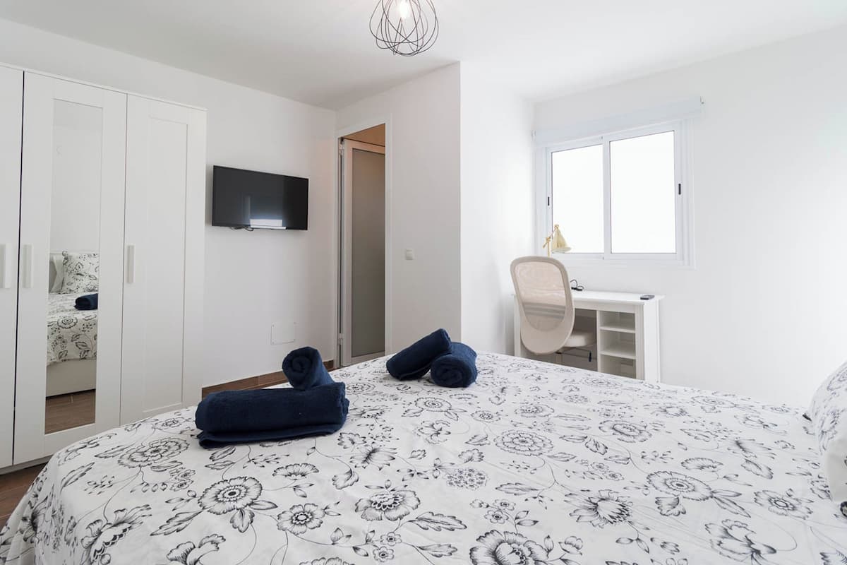 Quarto com cama, televisão, escrivaninha e cadeira.