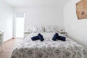 Quarto com colcha florida, duas toalhas enroladas na cama, mesa de cabeceira com abajur e porta que dá para uma varanda.